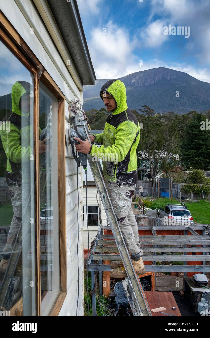 Painter on ladder doing surface preparation on a timber weatherboard ...