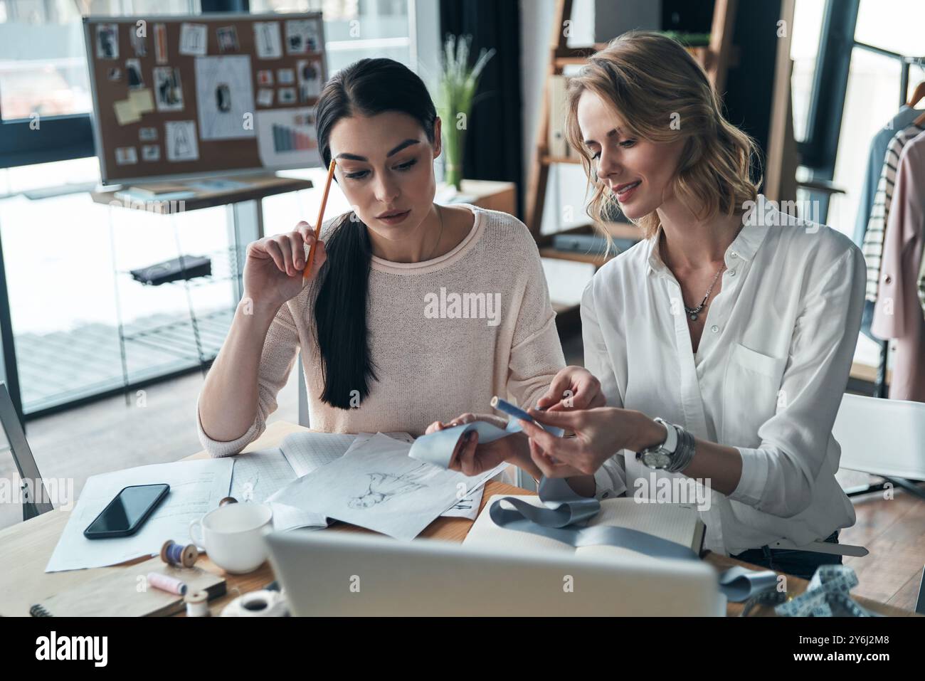 Designing new clothes. Beautiful young women working on sketches and ...