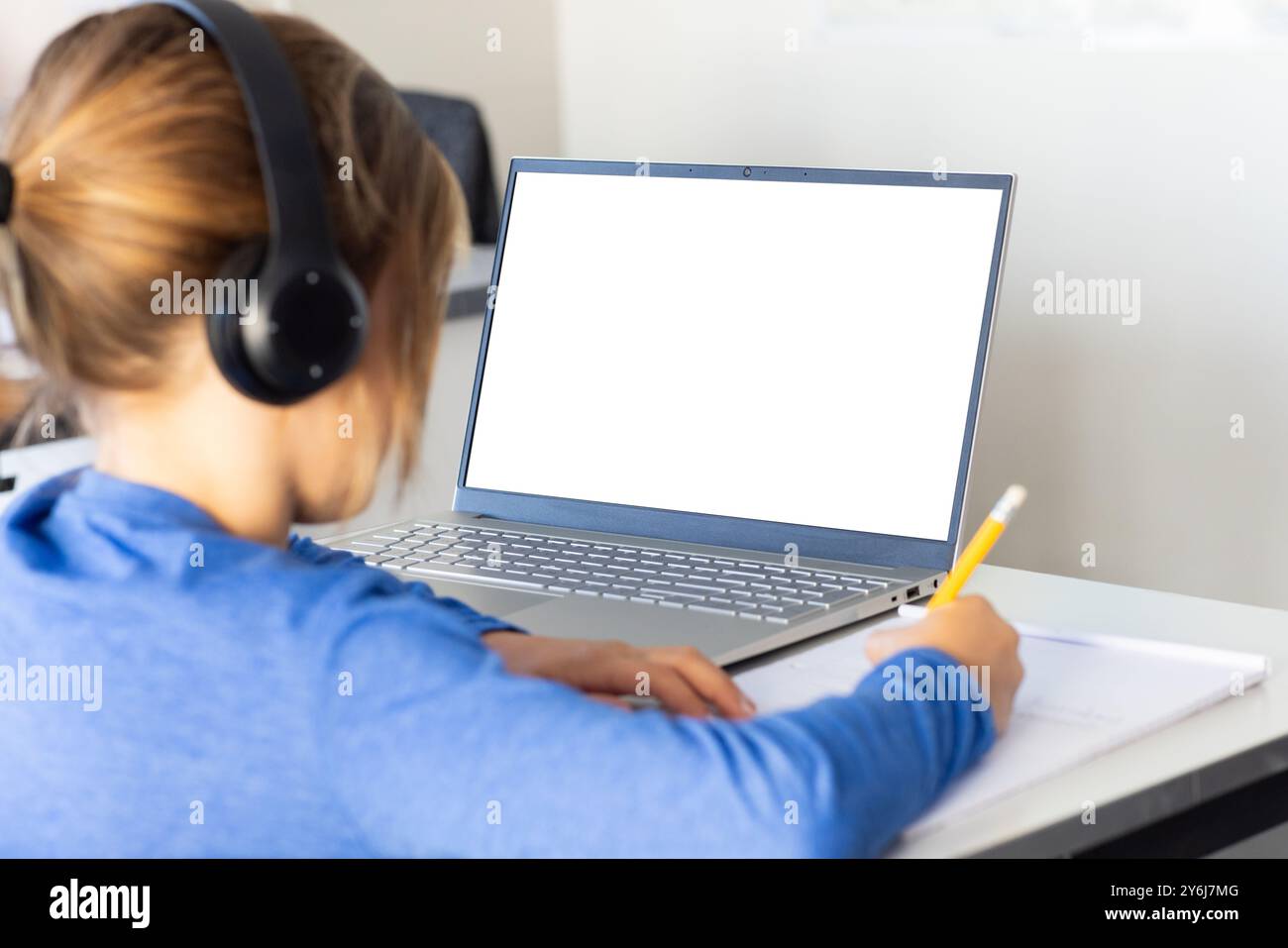 In school, boy wearing headphones writing in notebook while using ...