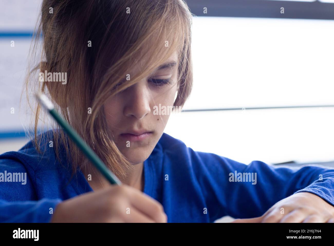 In school, focused boy writing with pencil in classroom, concentrating ...