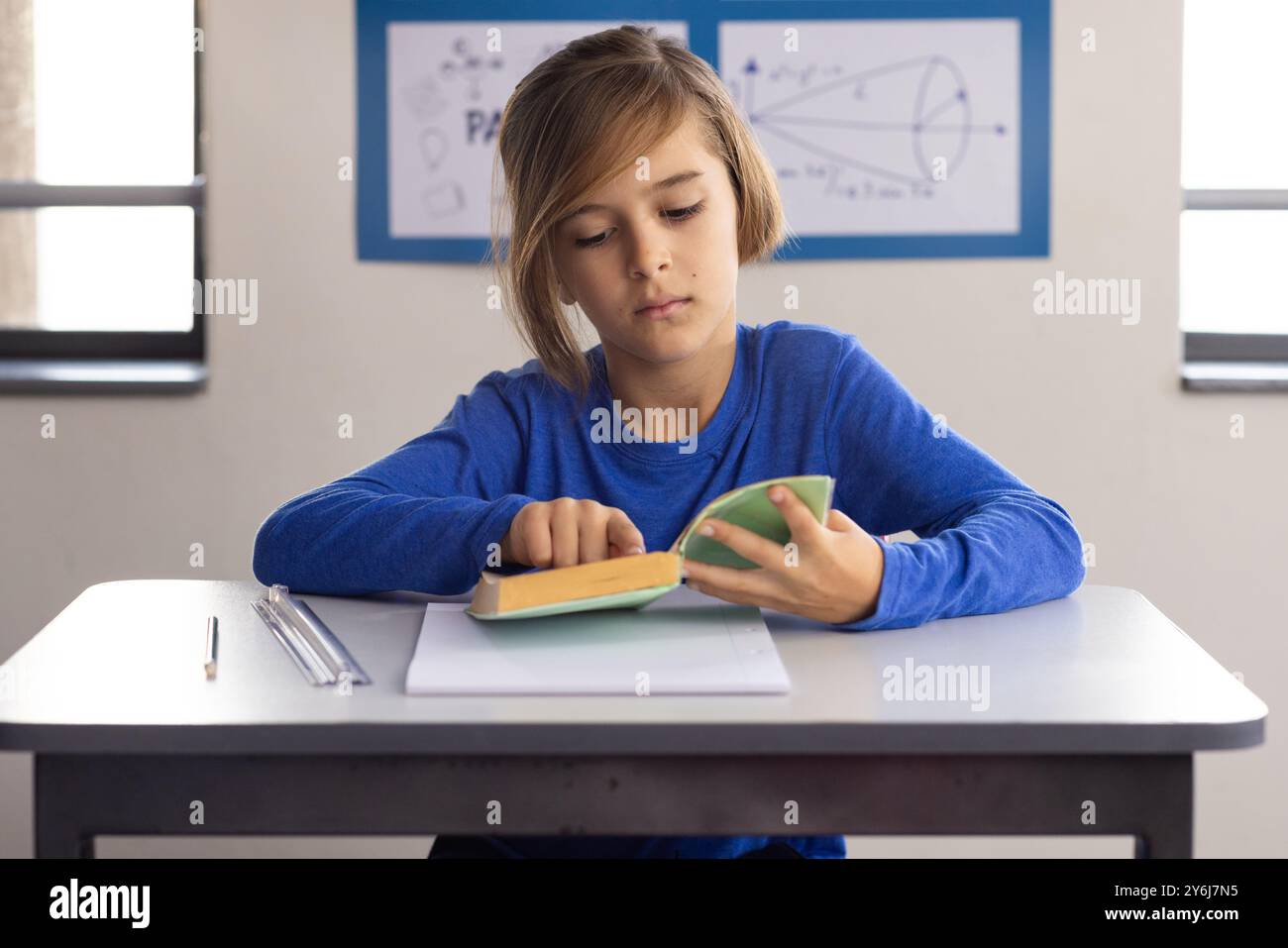 In school, boy reading book at desk, focusing on learning in classroom ...