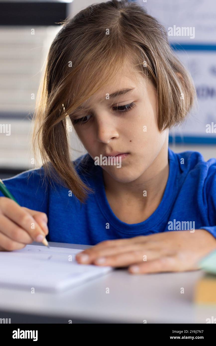 In school, focused boy writing in notepad during classroom activity ...