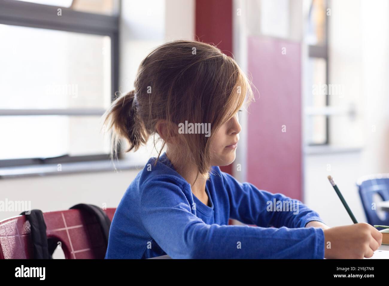 In school, boy writing with pencil in classroom, concentrating on task ...