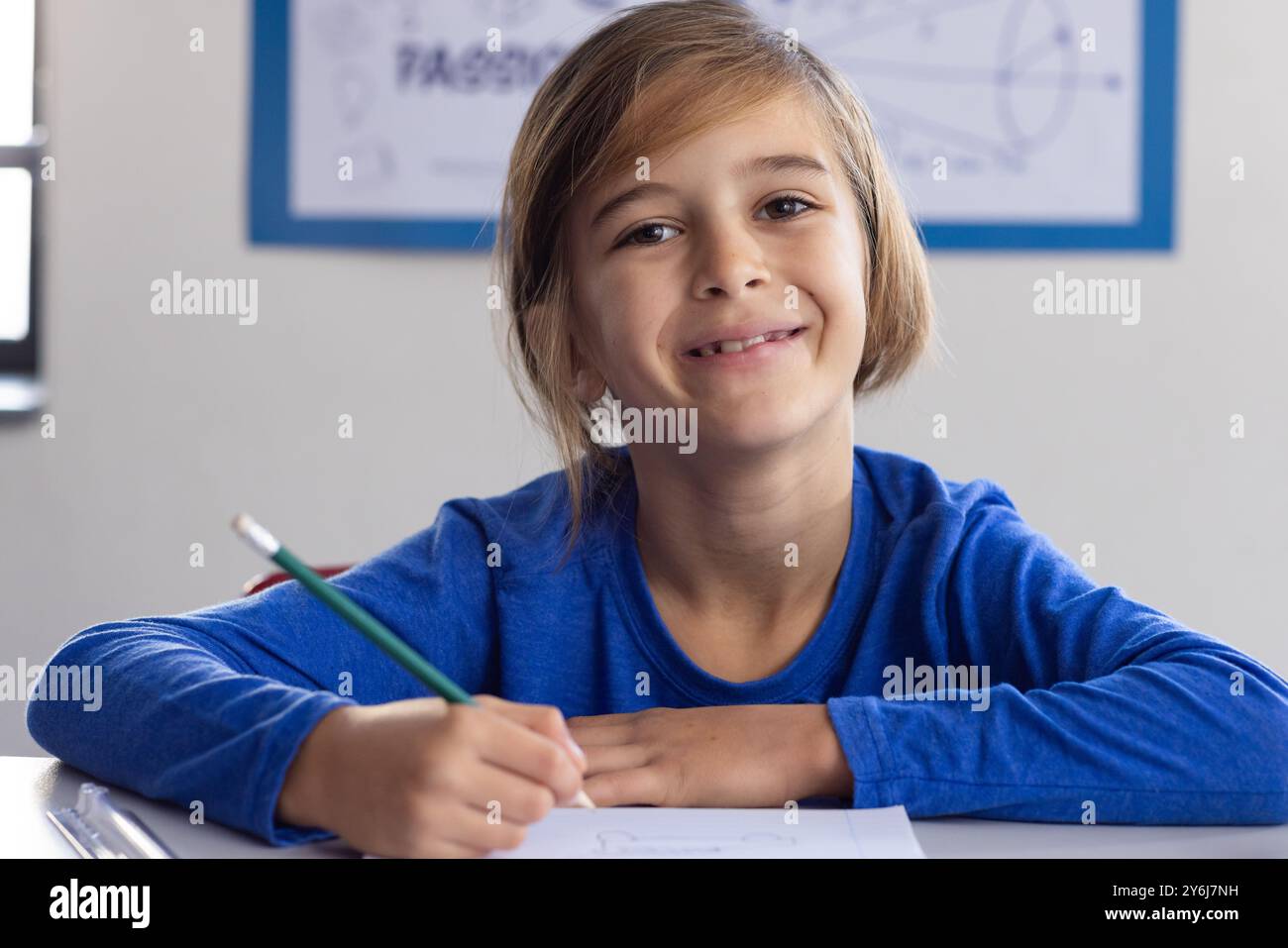 In school, smiling boy holding pencil and writing in classroom Stock ...
