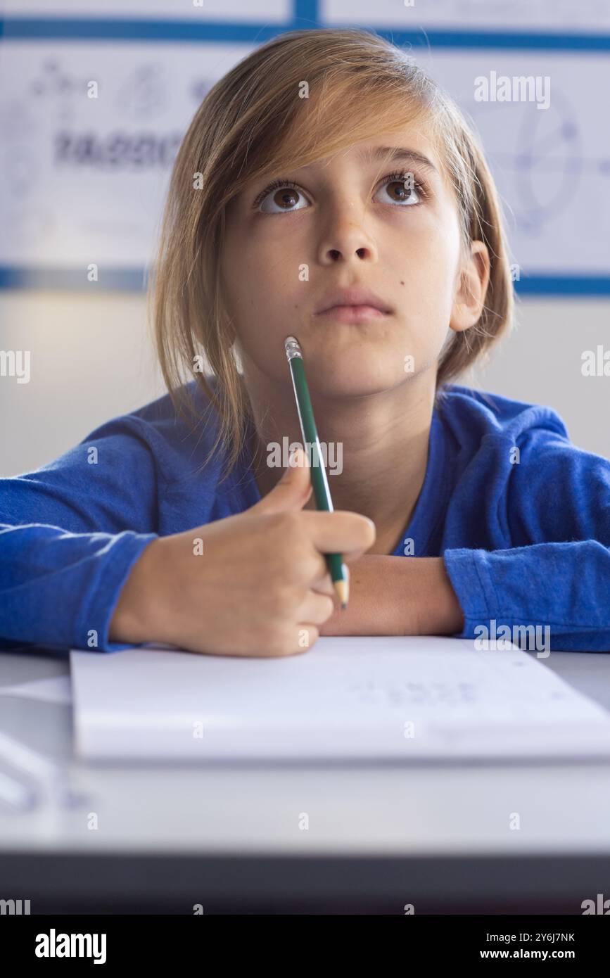 In school, boy holding pencil and thinking while looking up in ...