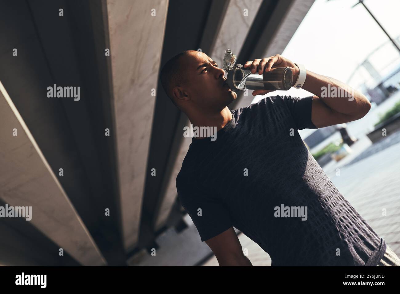 Hydrating. Young African man in sports clothing drinking water while ...