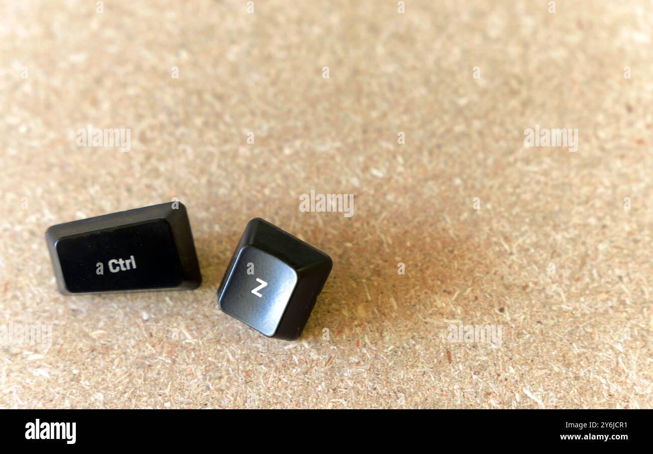 Two black keys are laying on a wooden surface. One of the keys is ...