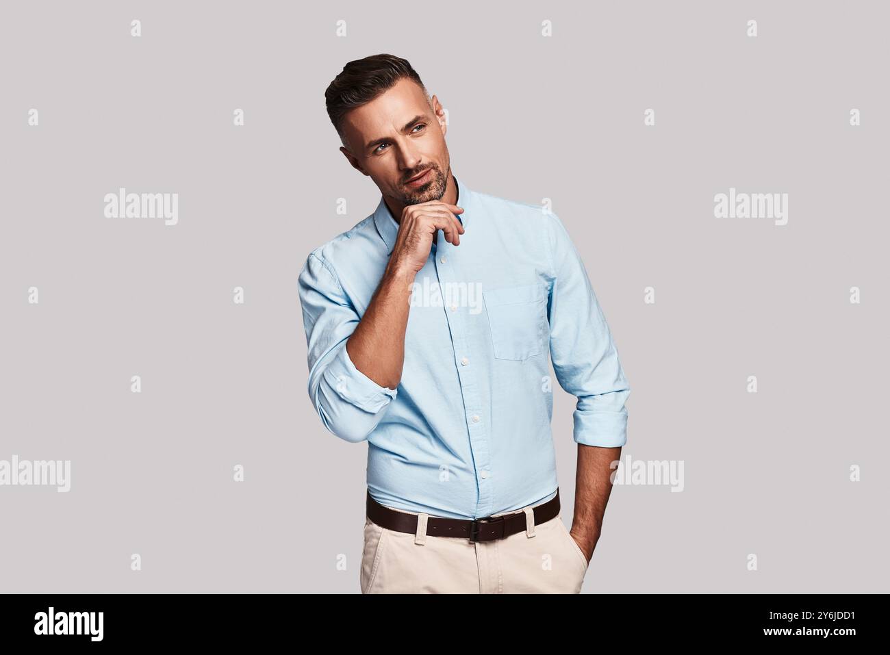 Searching for solution. Handsome young man keeping hand on chin and ...