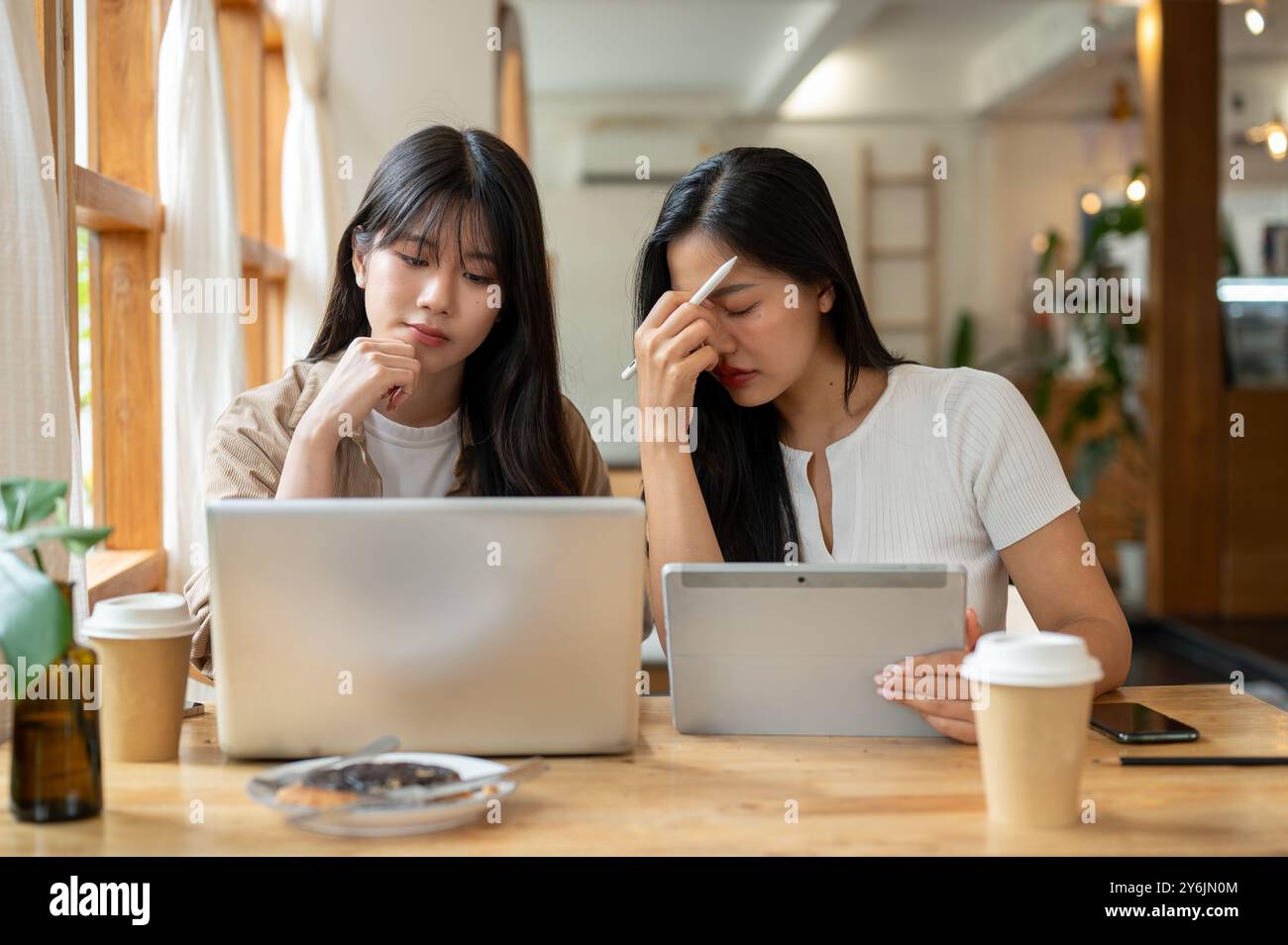 Two serious and stressed young Asian female friends are working ...