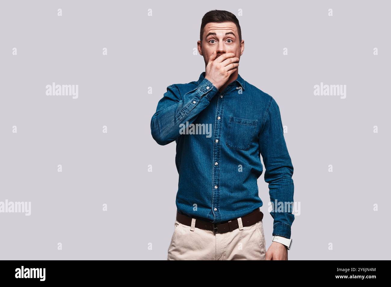 Shock. Surprised young man covering mouth with hand while standing ...