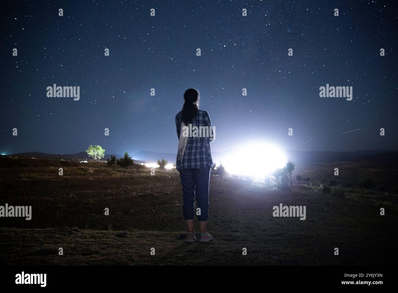 Woman gazing at a starry night sky illuminated by bright lights in a ...