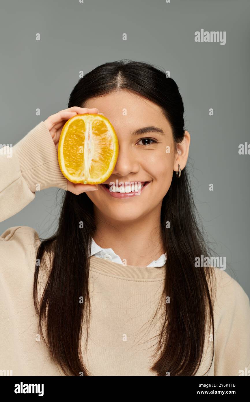 A young woman with long hair playfully covers one eye with an orange ...