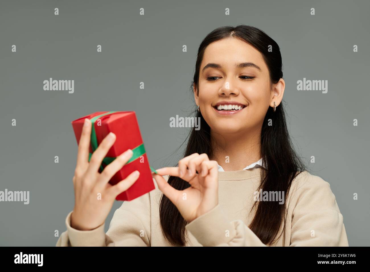 A stylish young woman unwraps a vibrant gift, joyfully expressing her ...