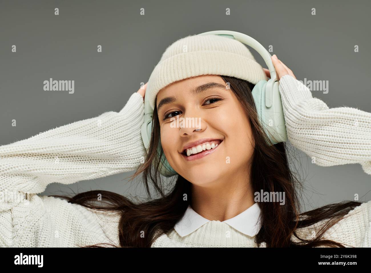 A cheerful young woman wearing a cozy sweater and headphones smiles ...