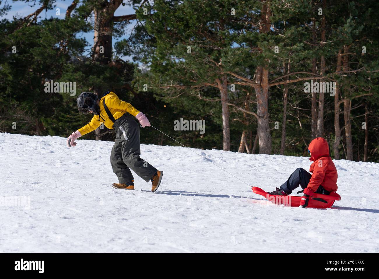 Two children playing in the snow with a sled, one pulling the other ...