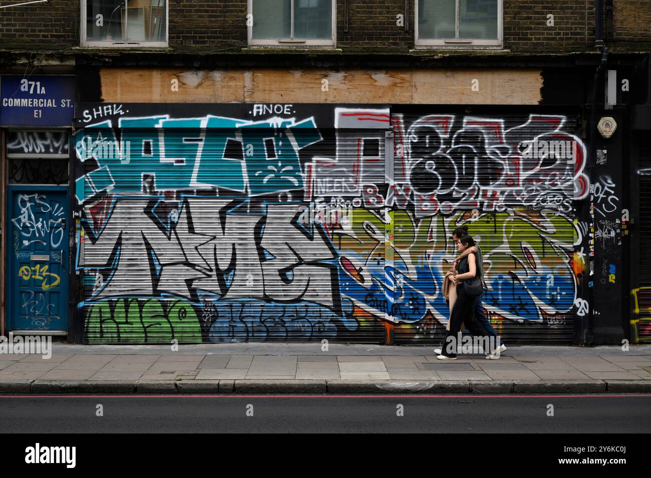 People walking past a graffitied roller door, Commercial Street, London ...