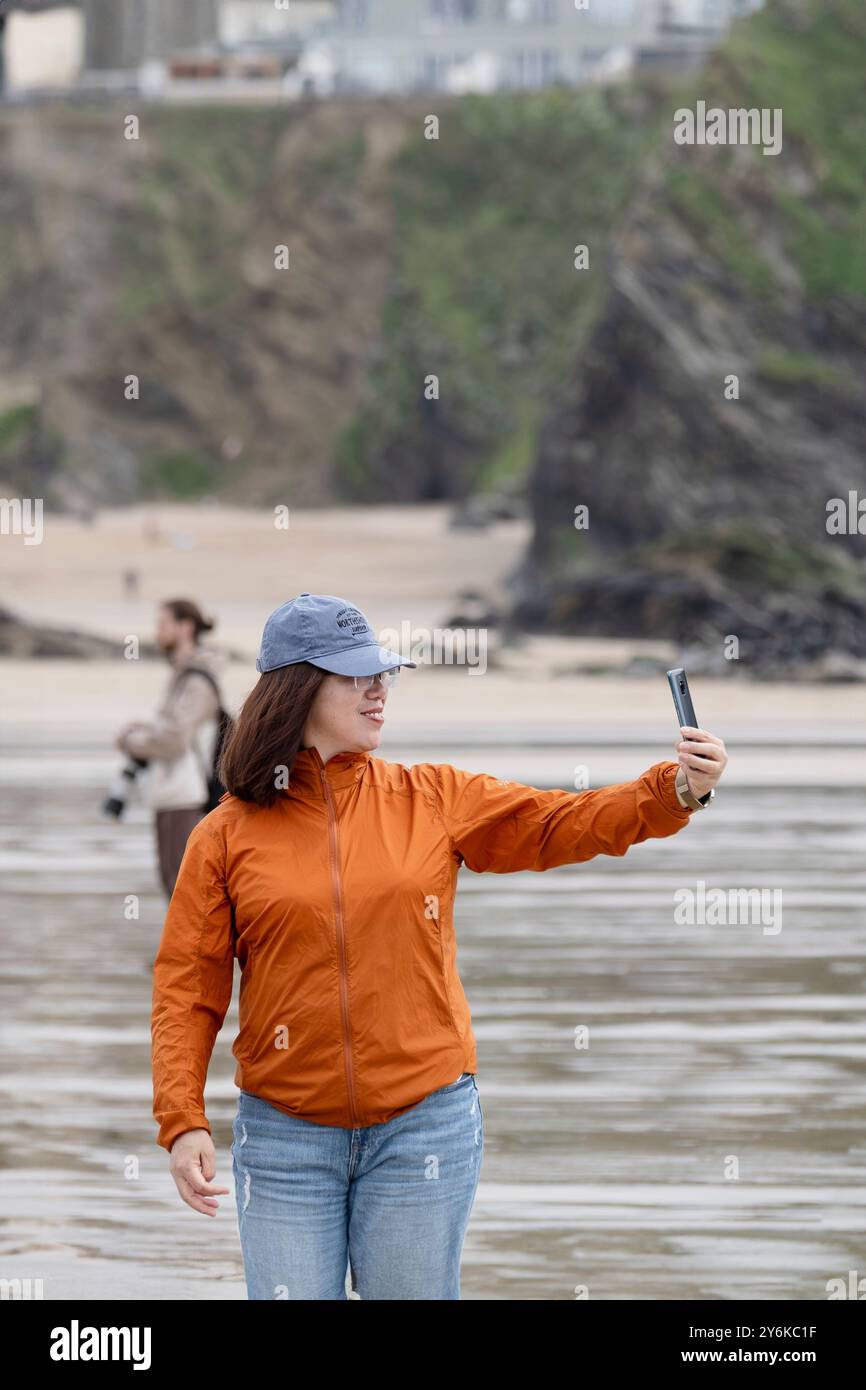 A visitor holidaymaker using her smart phone to take capture a selfie photograph on Towan beach ...