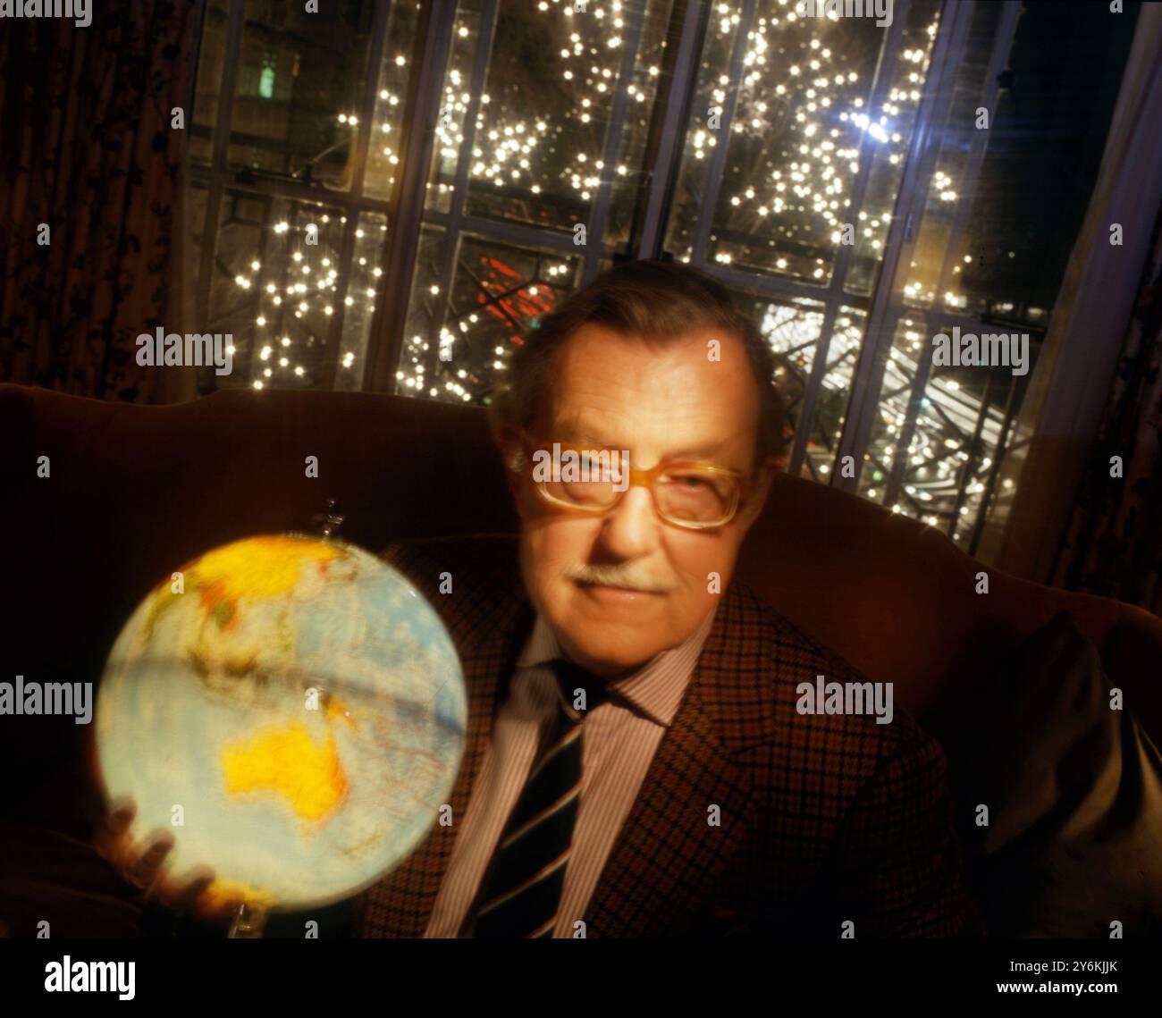Portrait of British journalist Alan Whicker holding a globe in London ...