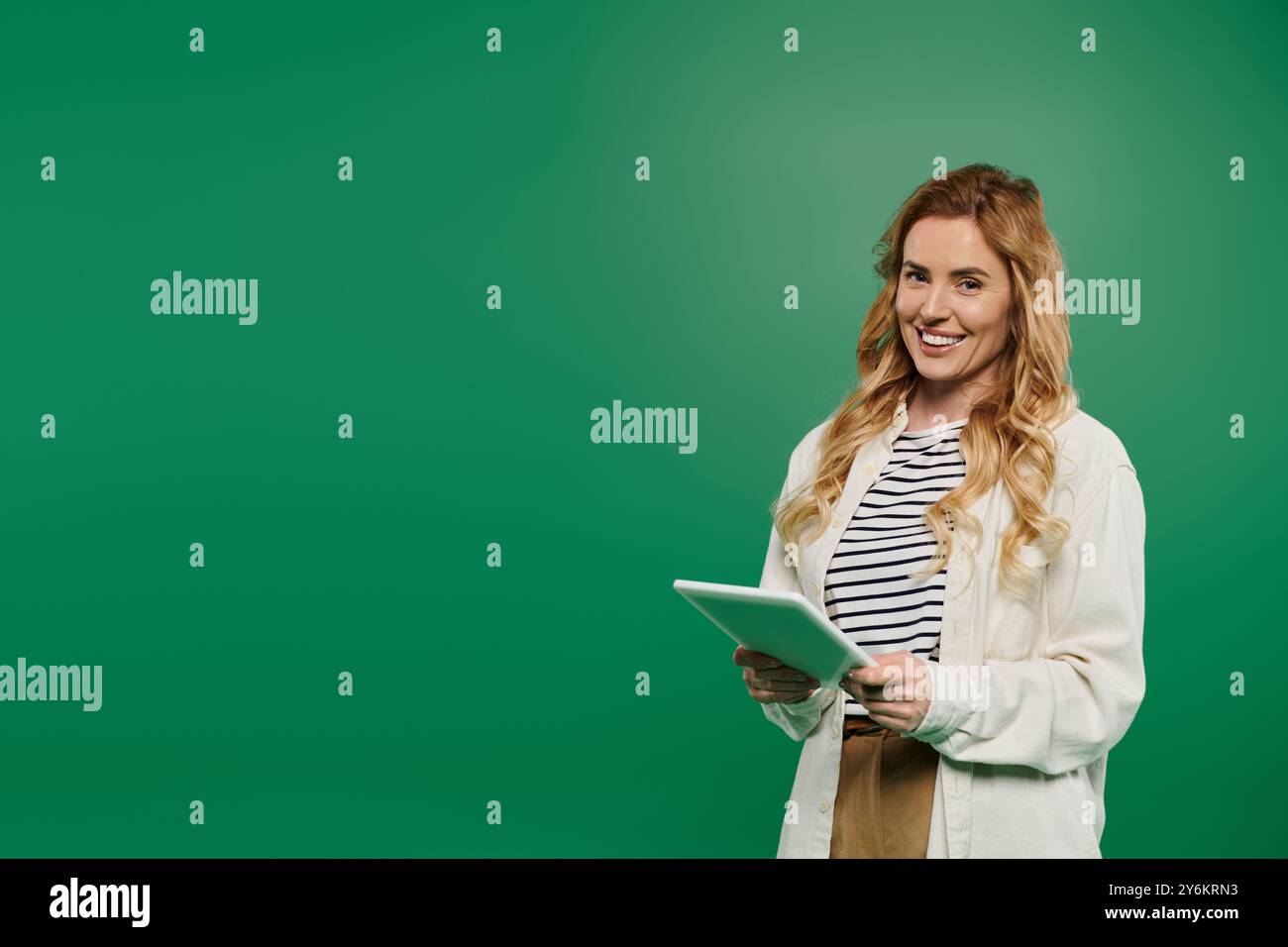 A joyful woman stands confidently, interacting with a tablet while ...