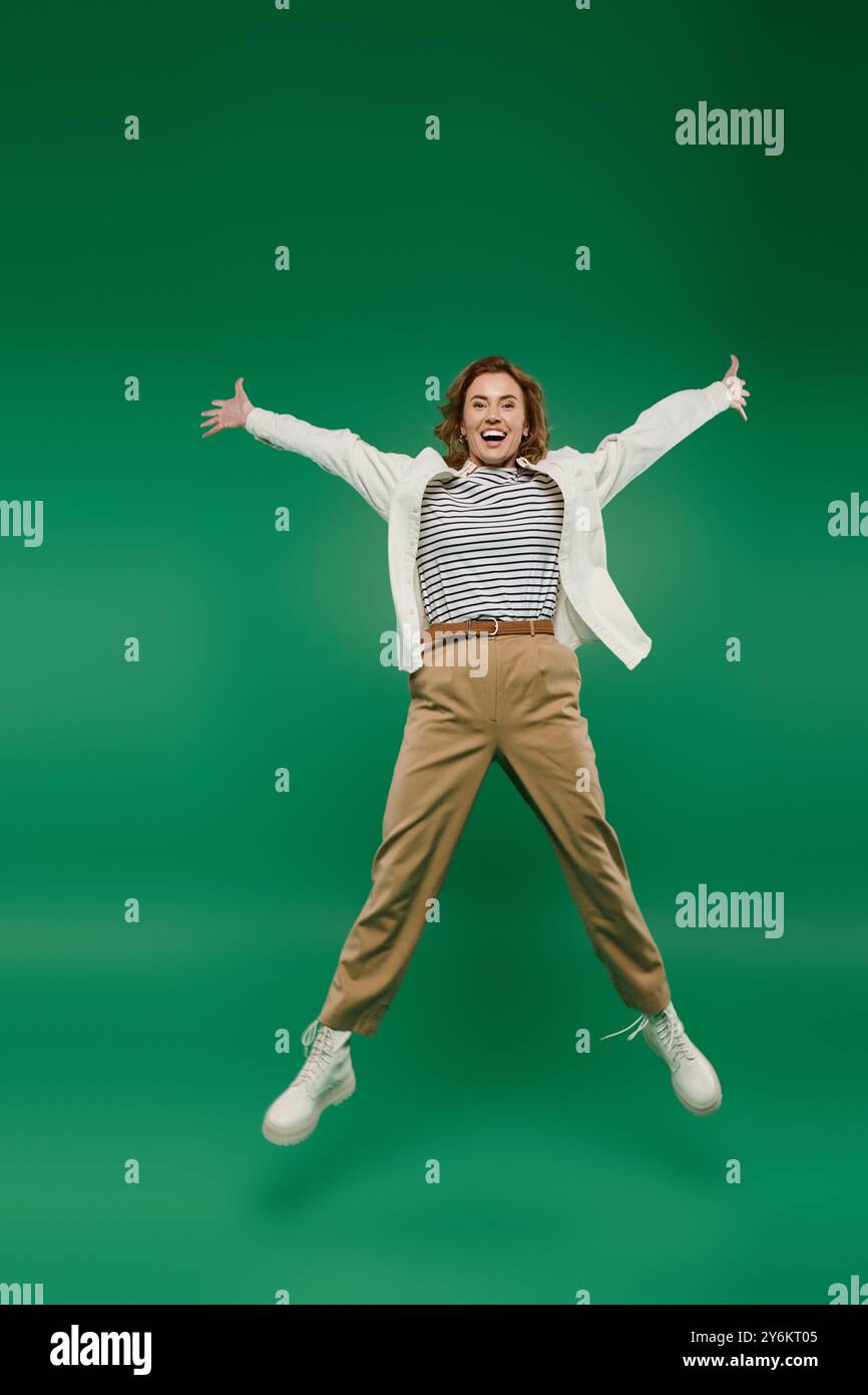 A cheerful woman with curly hair exudes happiness as she jumps on a ...