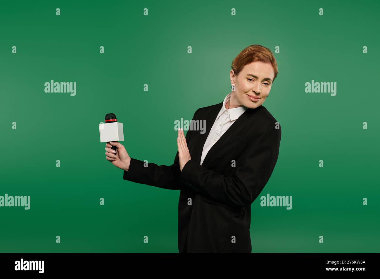 A poised TV presenter stands ready to engage, holding a microphone, set ...