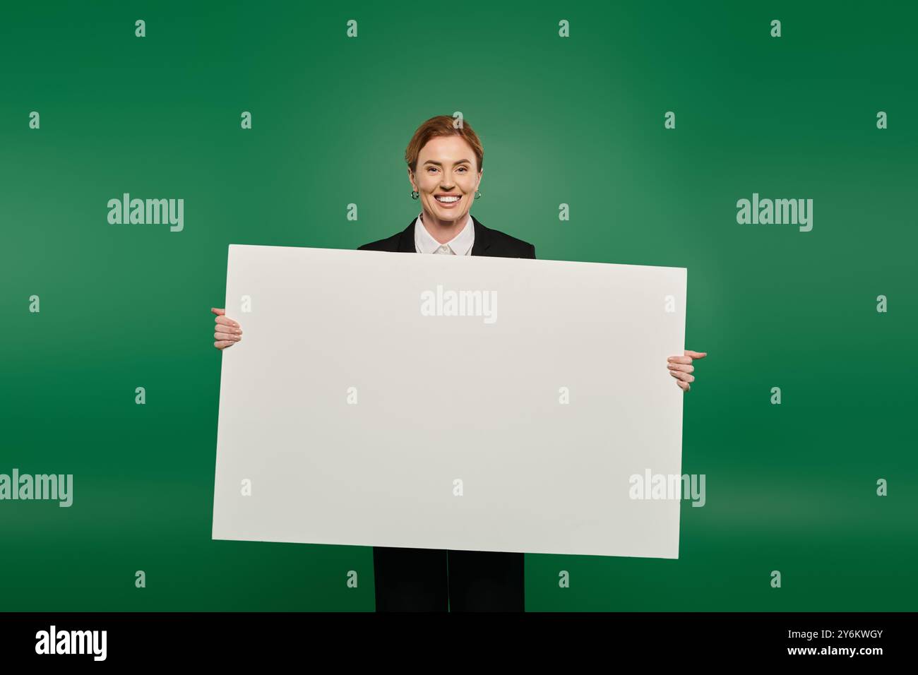 A charming presenter in a black suit holds up a blank sign against a ...