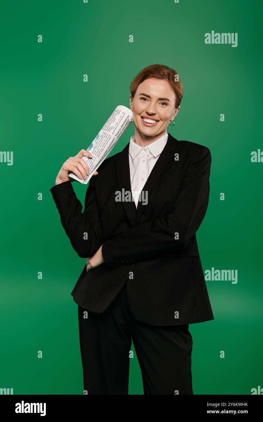 A confident TV presenter in black formal attire smiles while holding a ...