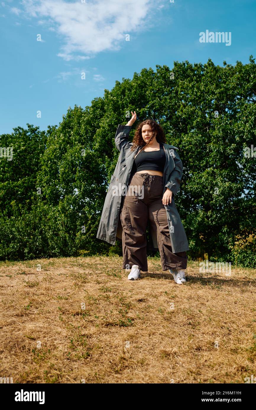 A confident plus size woman strikes a pose in a sunny field, enjoying ...