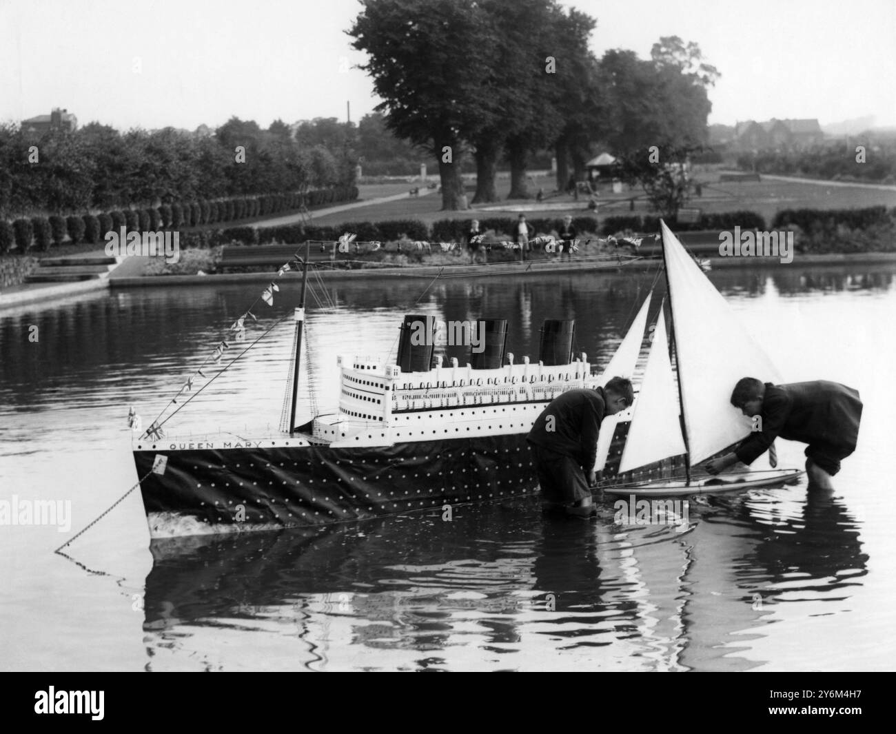 Boys sailing model yacht next to the model ship Queen Mary Stock Photo ...