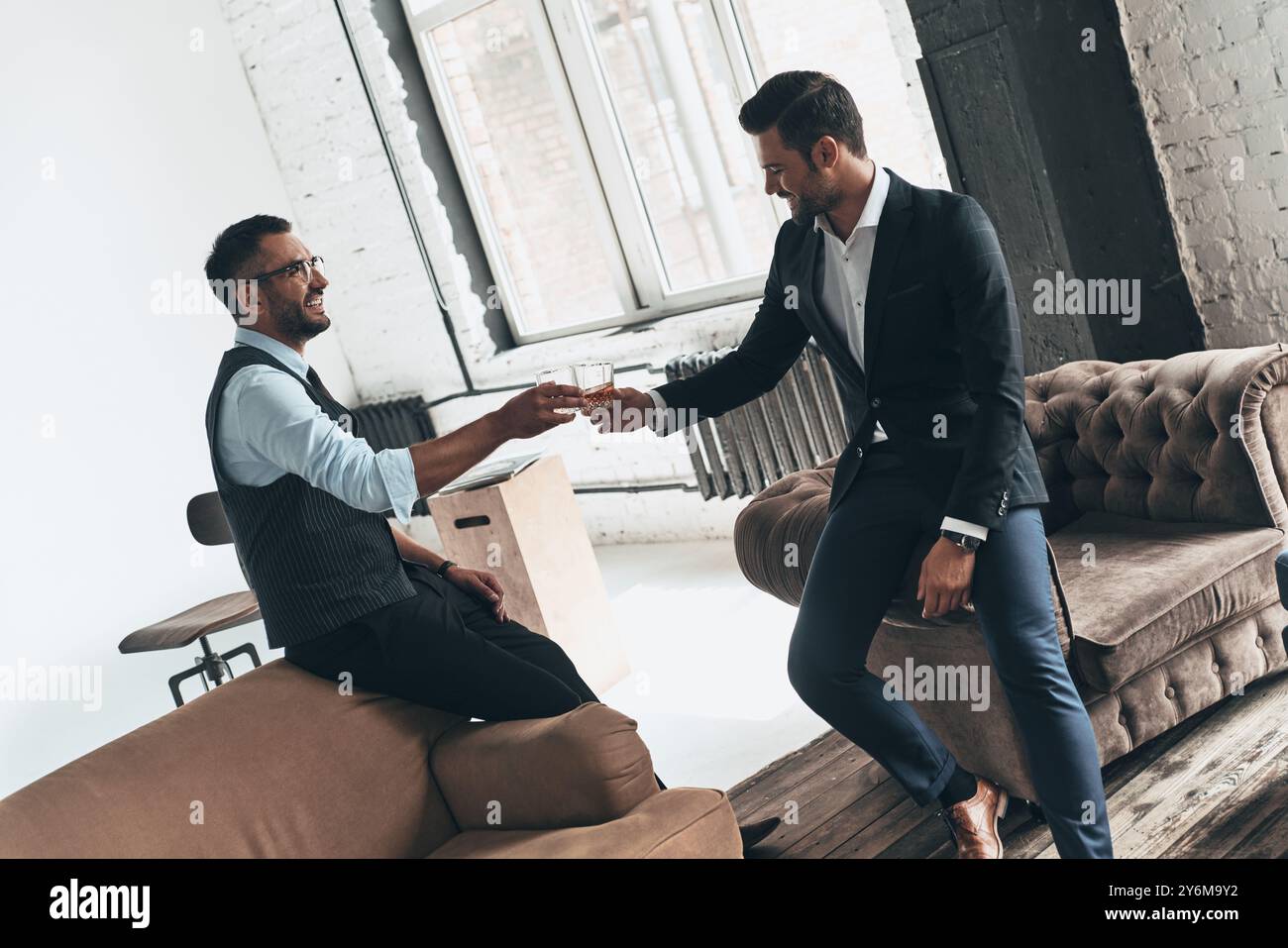 To friendship! Two young handsome men in suits toasting each other and ...