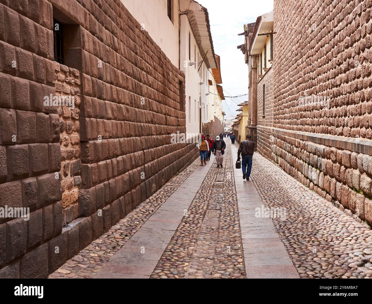 People stroll down a narrow cobblestone street in Cusco, Peru, flanked ...