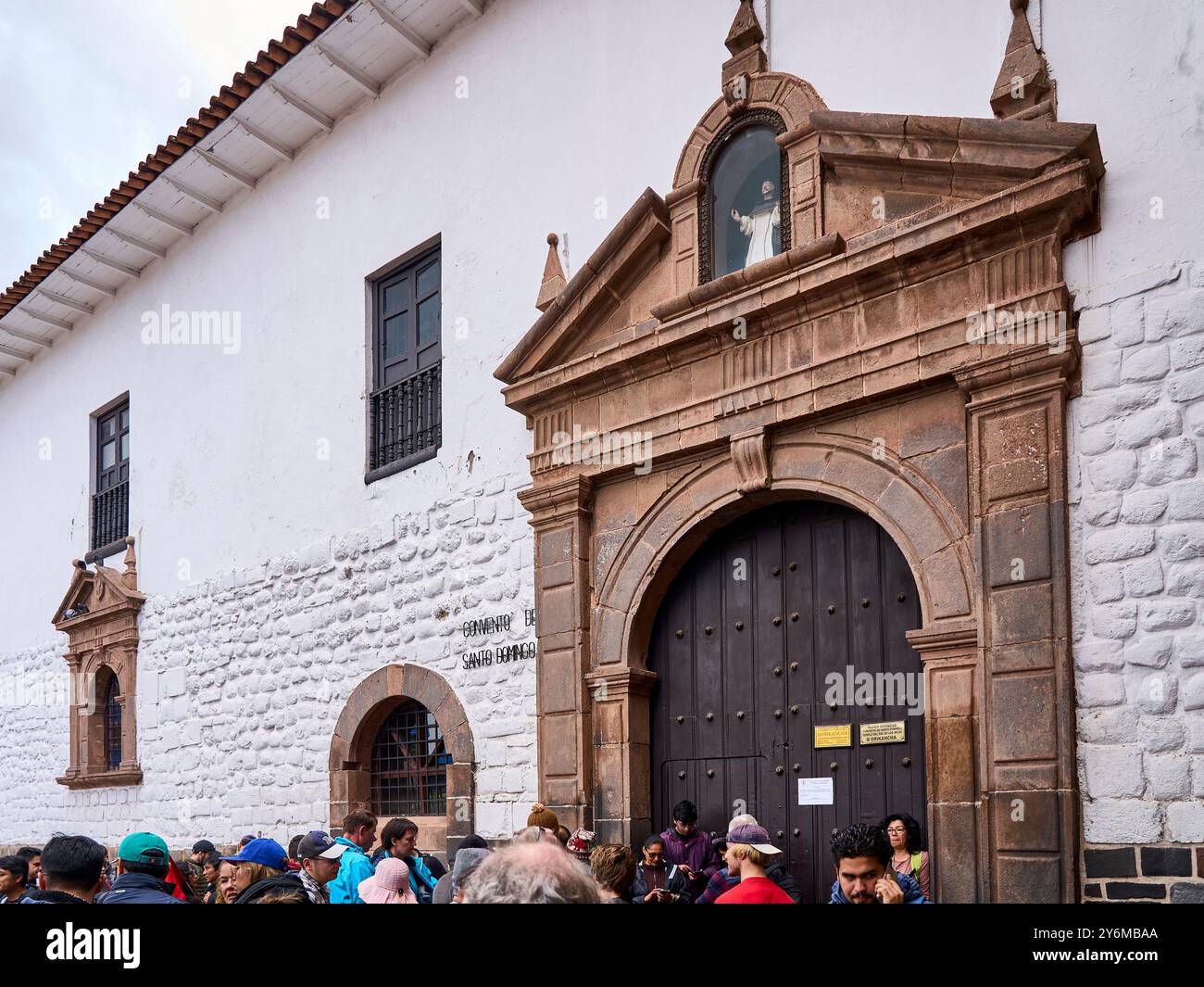 A large group of people gathers outside a historic stone building in ...