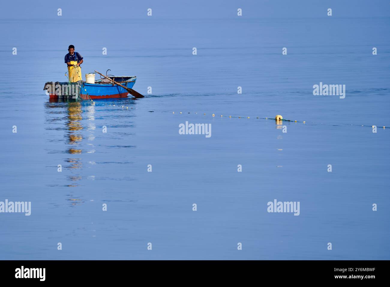 A fisherman handling nets on a small boat in calm, blue waters. The ...