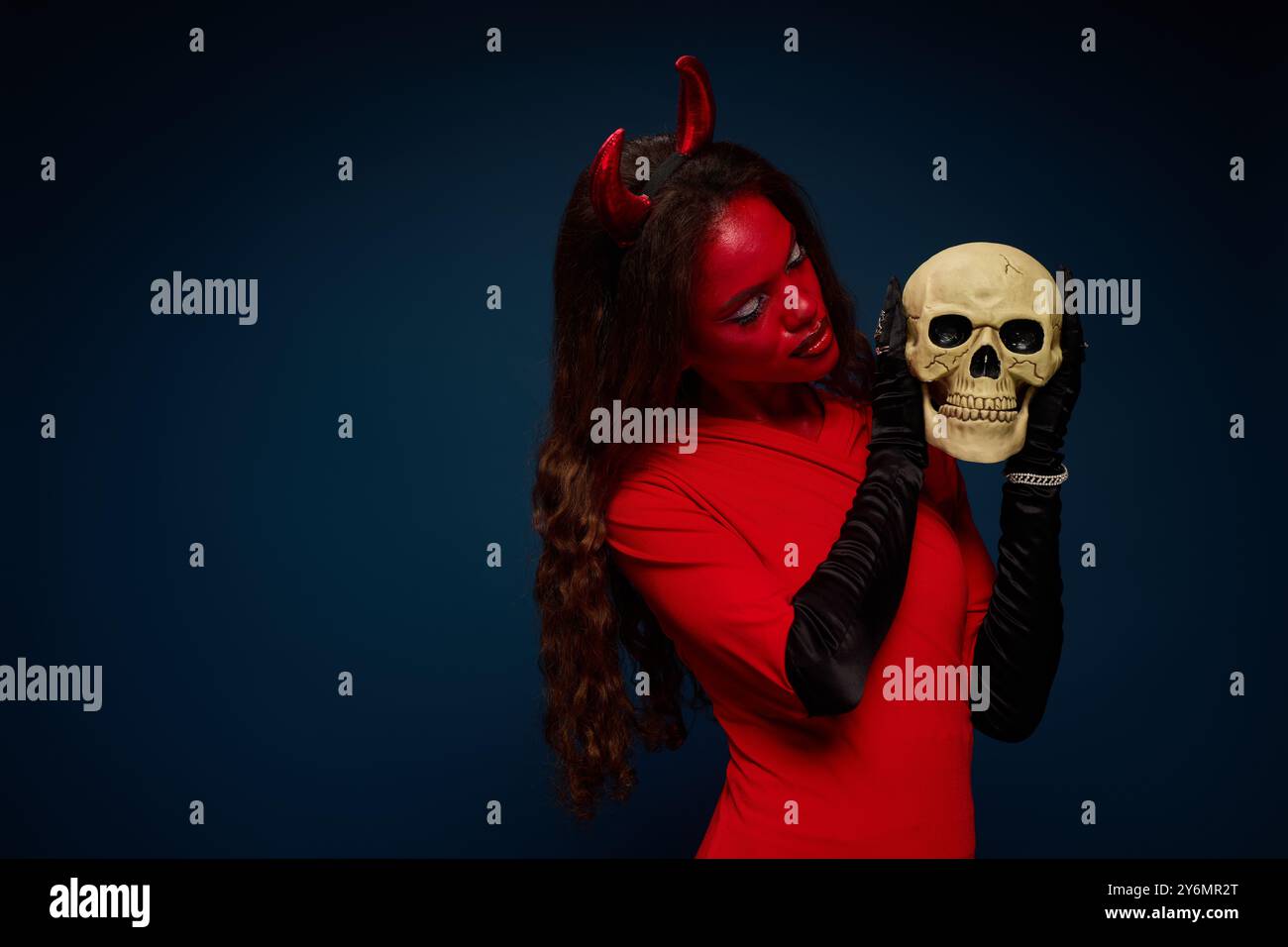 A stunning woman in a devil outfit passionately examines a skull ...