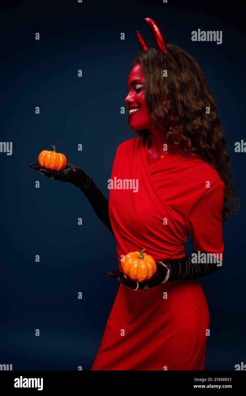 The beautiful woman dressed as a devil joyfully presents pumpkins ...