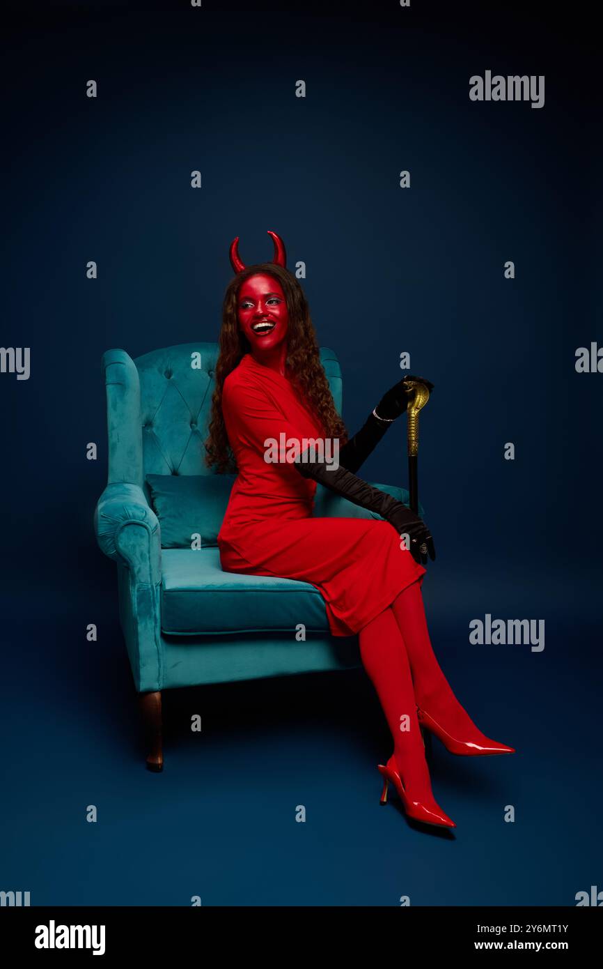 A stunning woman in a bright red devil costume sits confidently in a ...