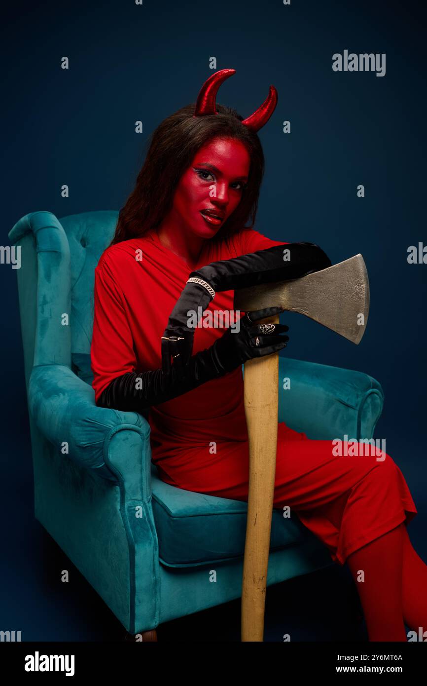A captivating woman dressed as a devil lounges in a plush blue chair ...