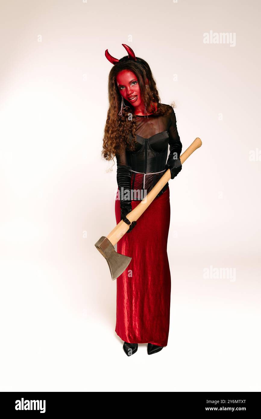 A beautiful woman in a devil costume poses confidently with an axe ...