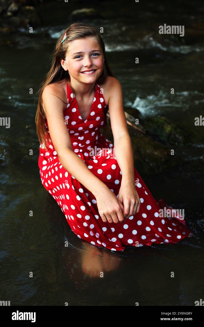 Beautiful young girl sitting on a rock in the river smiling Stock Photo ...