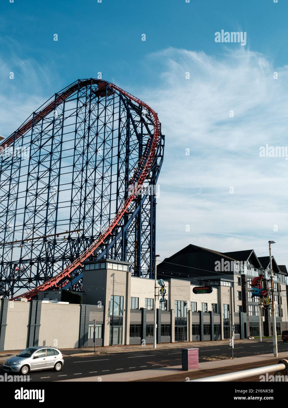 A towering roller coaster looms over urban architecture under a clear ...