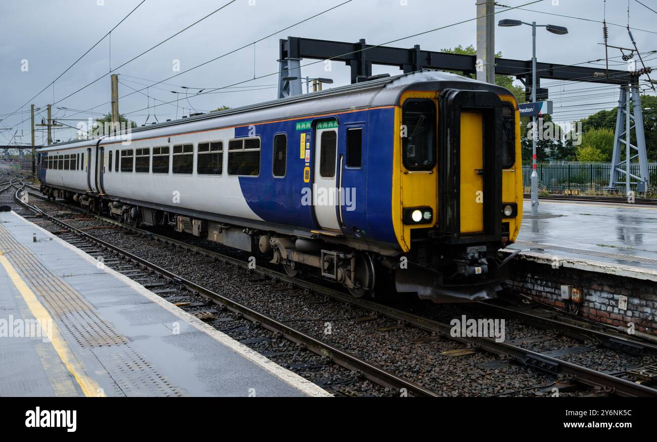 A diesel commuter train at a station, gleaming under overcast skies ...