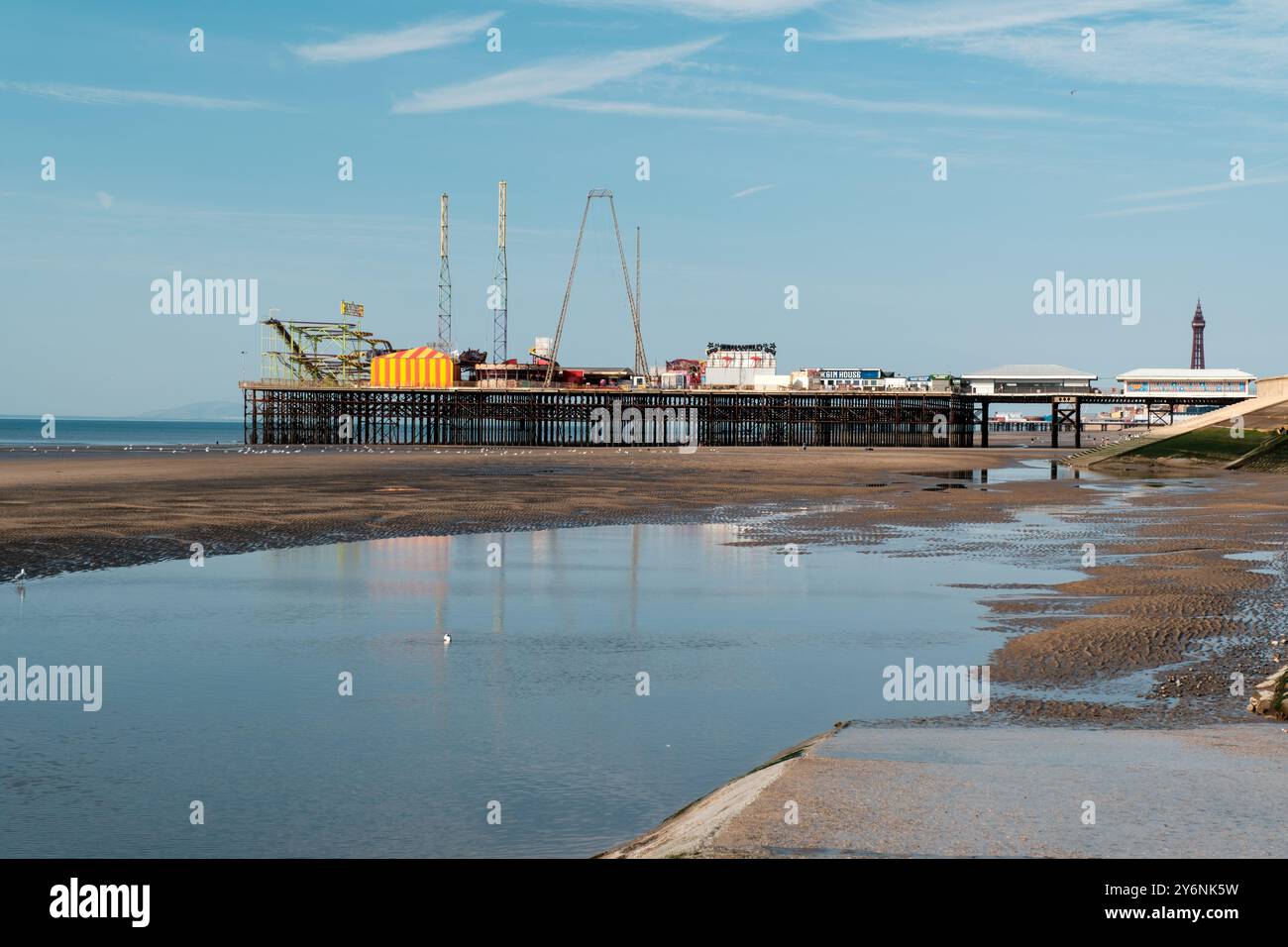 Serene view of an amusement pier with rides over a reflective wet beach ...