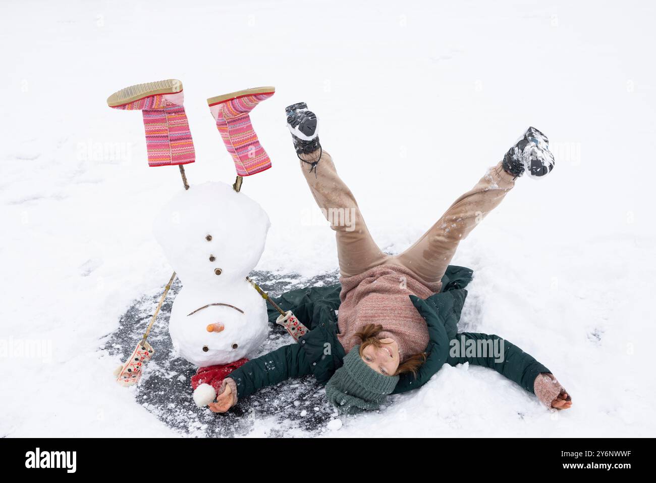 snowman in boots stands upside down in the snow, a cheerful young woman ...