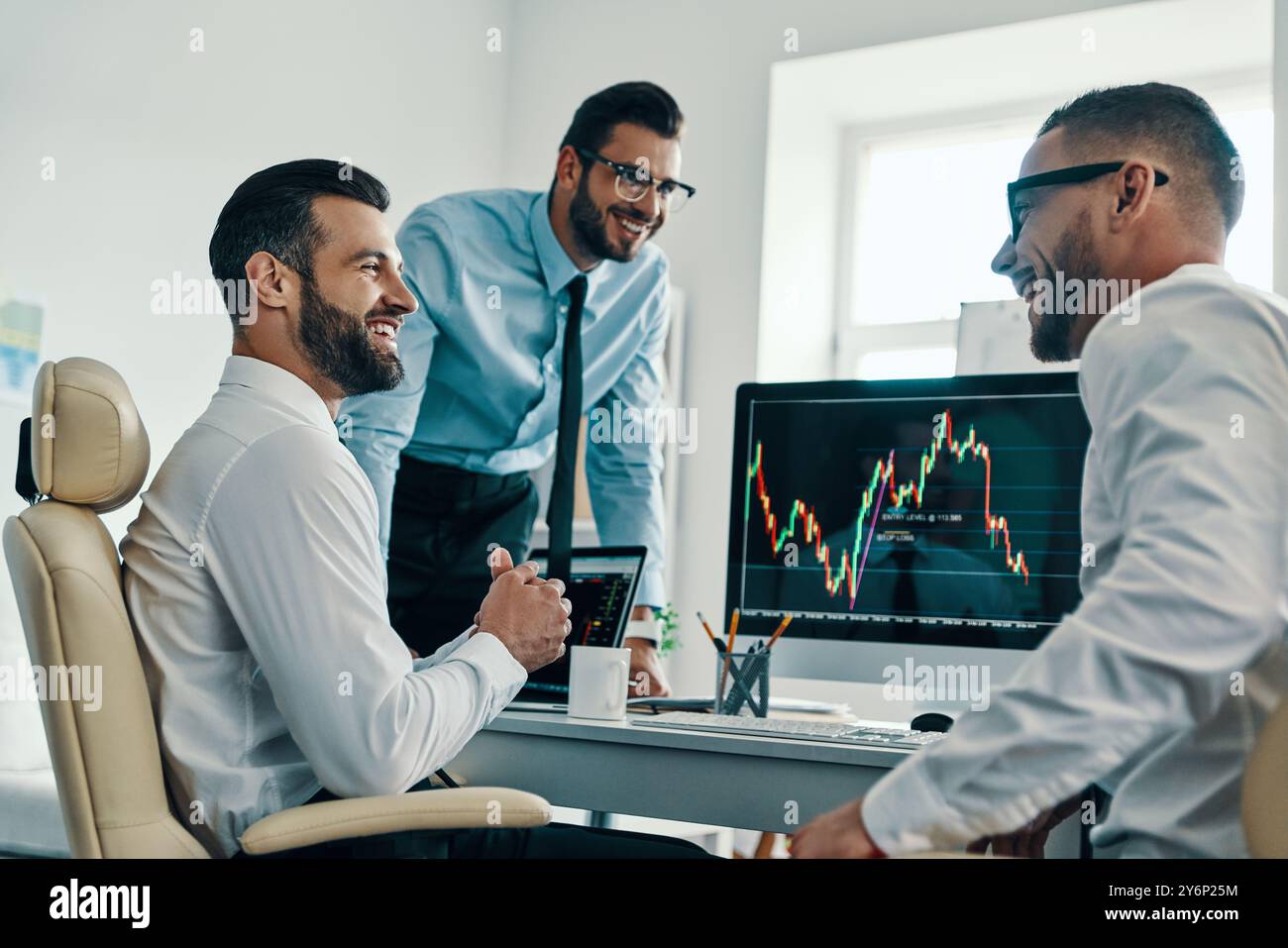 Successful traders. Group of young modern men in formalwear analyzing stock market data while ...