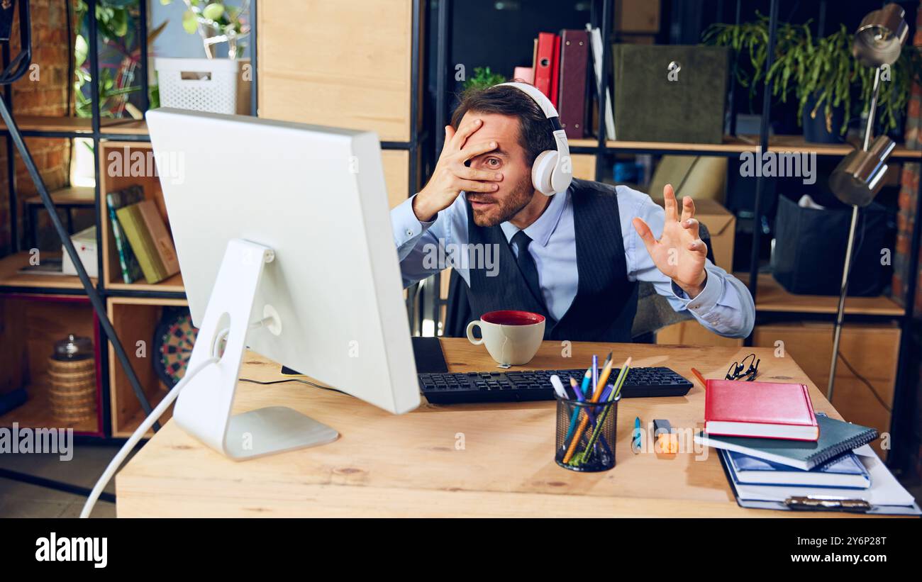 Overwhelmed by what's on screen, man covers his face, peeking through ...