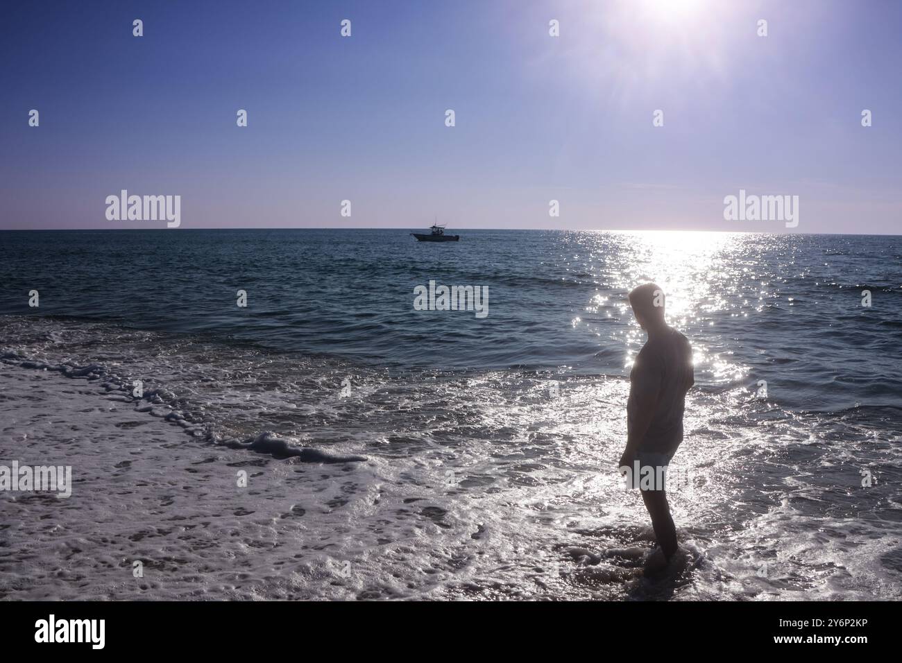 Reflective young man observes a boat in the sea from the shore of the ...