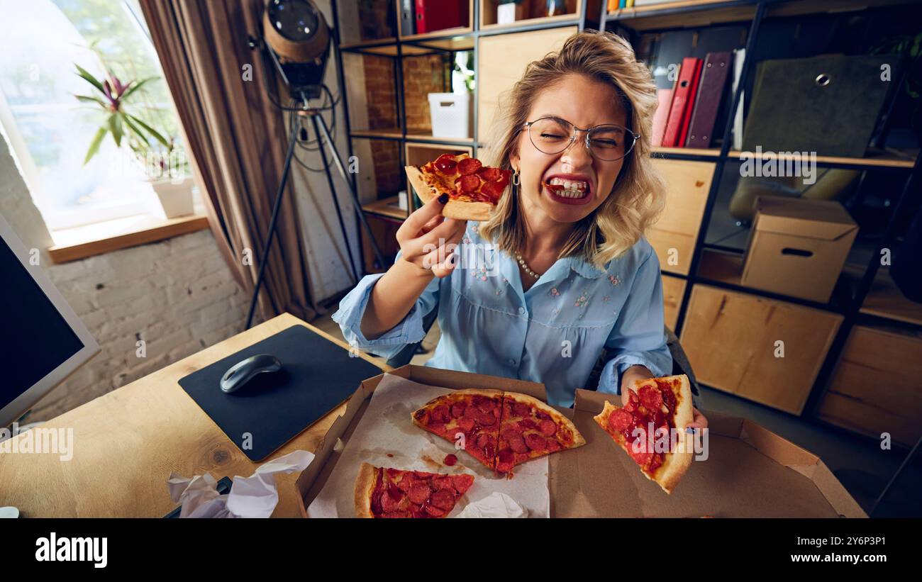 Woman showing her pizza slice triumphantly, looking into camera ...