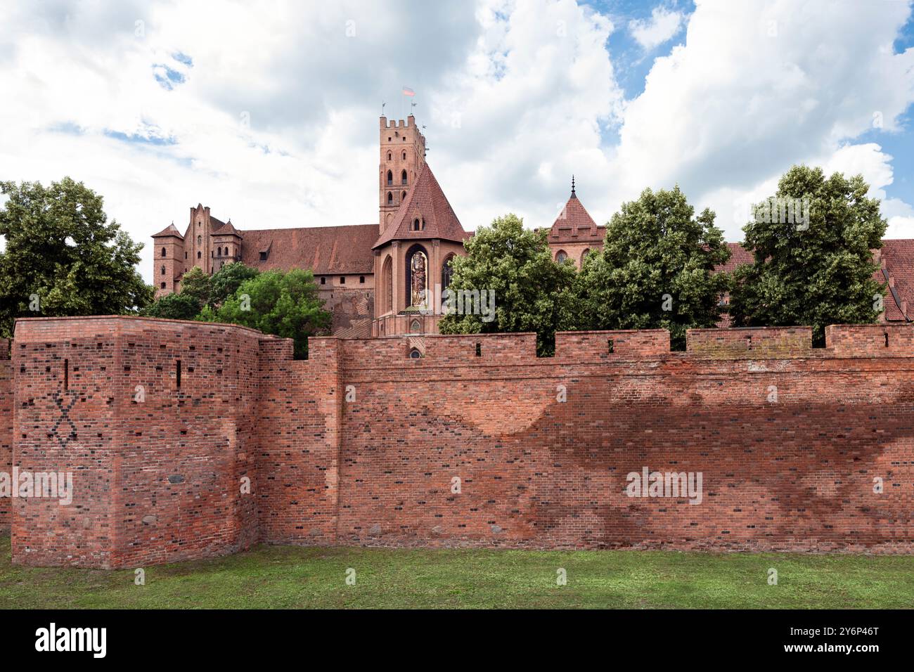 Red brick and roof medieval castle behind a defense wall and trees ...