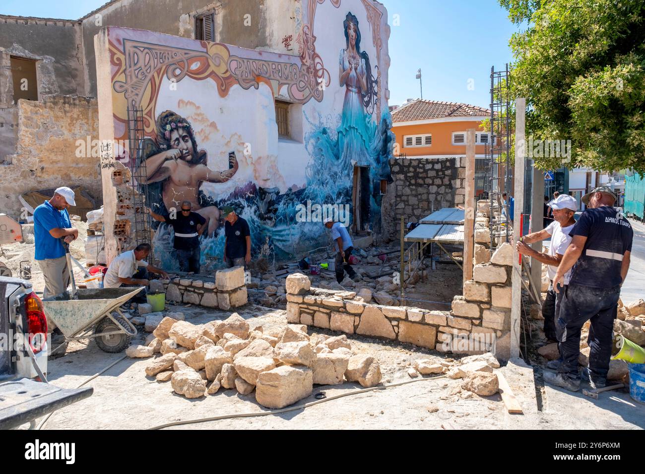 Workmen building a stone wall beside a colourful wall mural in Paphos ...