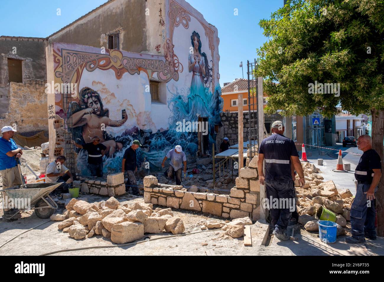 Workmen building a stone wall beside a colourful wall mural in Paphos ...